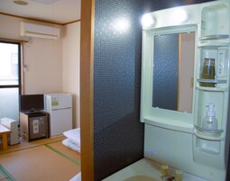 Casa de banho com lavatório, espelho e artigos de higiene. Tem televisão e um frigorífico pequeno no canto.