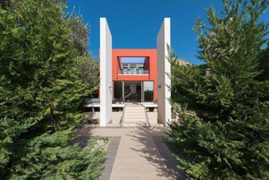 Uma casa moderna com fachada vermelha, entrada de vidro e um caminho que leva à porta da frente.