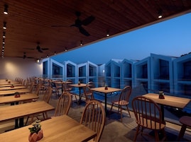 Um restaurante com mesas e cadeiras de madeira, um ventilador de teto e vista para o céu.