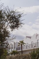 Um edifício moderno com fachada branca, várias varandas e uma palmeira em primeiro plano.