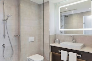 Casa de banho moderna com chuveiro, sanita, lavatório e espelho.