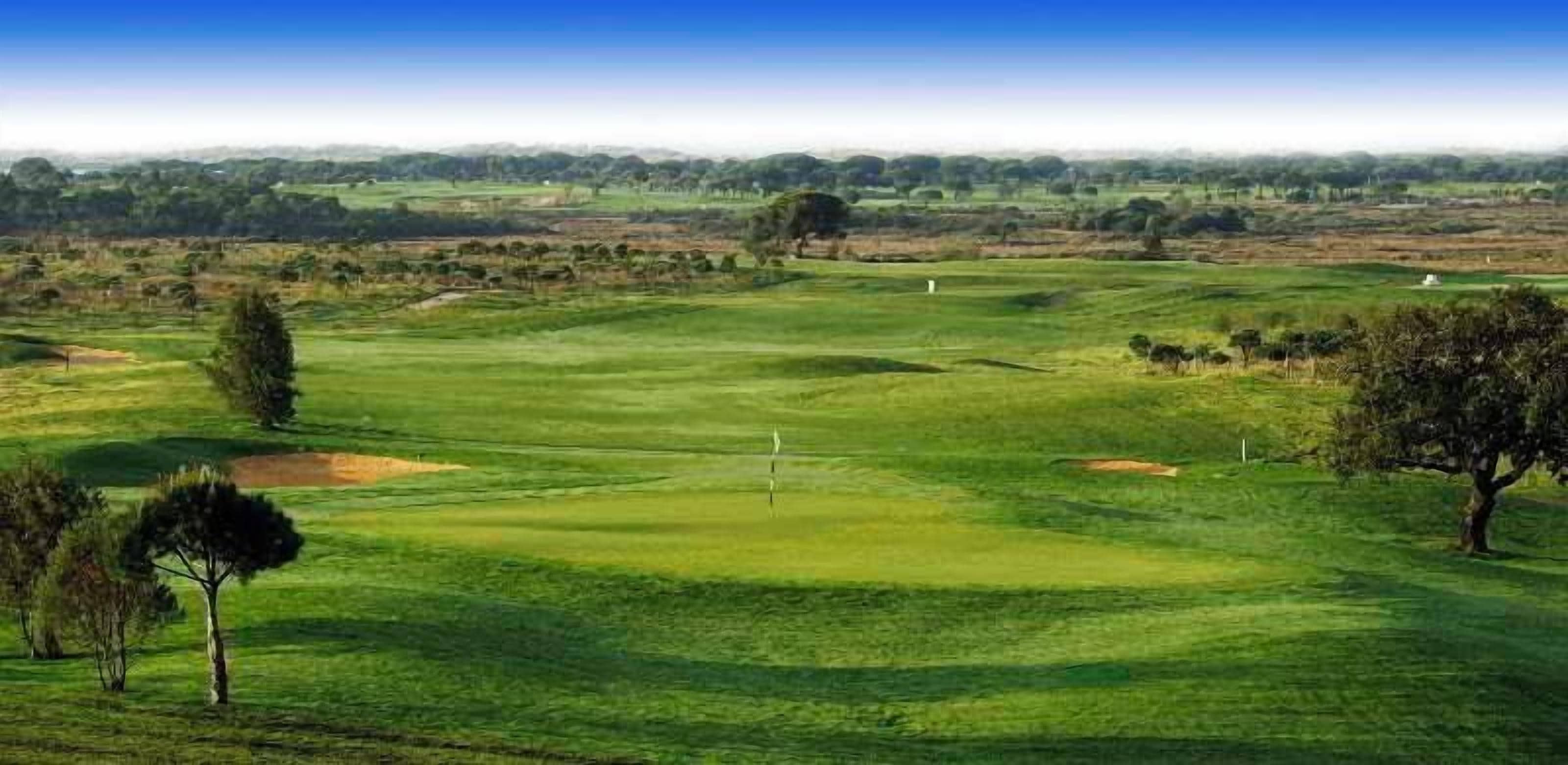 Um campo de golfe com vista clara para o fairway, bunkers de areia e um mastro de sinalização.
