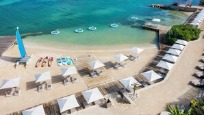 Vista aérea de um resort à beira-mar, com espreguiçadeiras, guarda-sóis e um deck de madeira.