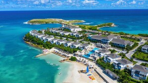Vista aérea de um resort à beira-mar, com vários edifícios, praia e águas azul-claras.