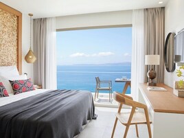 Quarto de hotel com uma cama grande, uma escrivaninha com cadeira, televisão e vista para o mar.