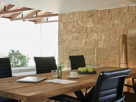 Sala de conferência com mesa de madeira, cadeiras pretas, um laptop, uma garrafa, uma tigela de maçãs e um copo.