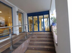 Escadaria que leva à entrada de um edifício, com porta azul e painéis de vidro.