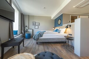 Quarto de hotel moderno com cama, mesas de cabeceira, escrivaninha e uma grande janela.