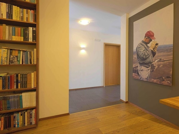 Um corredor com uma estante de madeira cheia de livros, uma porta de madeira e um quadro de uma pessoa com um gorro vermelho.