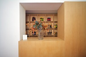 Uma vitrine de madeira com garrafas de vinho e um vaso com ramos e flores.