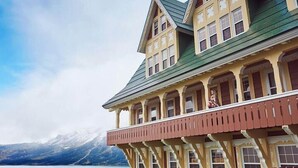 Um edifício de vários andares com varanda, telhado verde e vista para um lago e montanhas.
