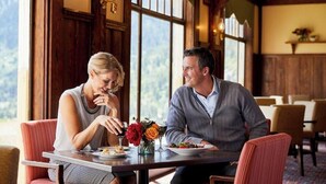 Um casal jantando à mesa com vista para o exterior, paredes de madeira e um candelabro.