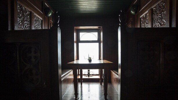 Um corredor estreito com uma mesa e cadeiras de madeira, que dá para uma janela com vista externa.