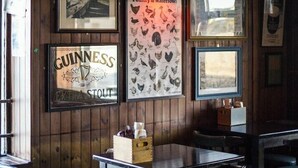 Interior de restaurante com paredes de madeira, placa de prancha de surf, quadros enquadrados e uma mesa com cadeiras.