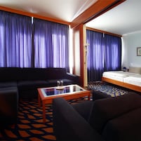 Quarto de hotel com sofá, cama, mesa de centro e carpete estampado.