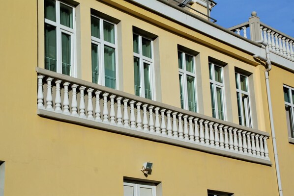 Um edifício amarelo com janelas emolduradas a branco e uma varanda com grades.