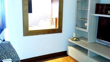Uma sala de estar moderna com uma janela emoldurada em madeira, um rack branco com livros e uma TV, e um sofá com estampa de leopardo.