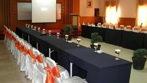 Uma sala de conferência com mesas compridas, cadeiras e uma tela de projeção.