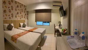 Quarto de hotel com duas camas, uma escrivaninha, uma cadeira, uma televisão e uma janela com vista.