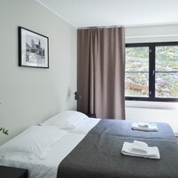 Quarto de hotel com cama, janela com cortinas, quadro na parede e radiador.