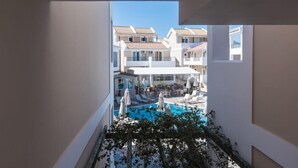 Vista de uma área de piscina com espreguiçadeiras e guarda-sóis, rodeada por edifícios com vários andares e varandas.