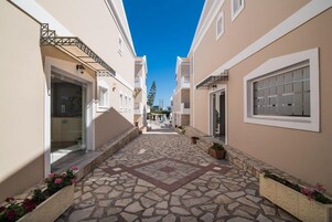 Uma rua estreita com calçada de pedra, edifícios de ambos os lados e floreiras ao longo do caminho.