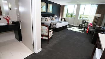 Quarto de hotel com uma cama grande, uma escrivaninha, uma cadeira, banheiro com pia e espelho, e vista para o exterior.