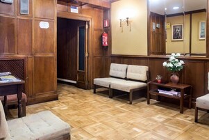 Um hall com piso de madeira, um sofá, uma pequena mesa com um vaso e um extintor de incêndio.