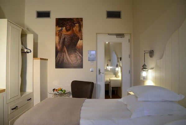 Quarto de hotel com cama, escrivaninha e cadeira, um quadro na parede e porta de acesso a um banheiro.
