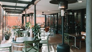 Um café interior com mesas redondas, cadeiras verdes e plantas em vasos.