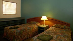 Quarto com duas camas, mesa de cabeceira com abajur e janela com persianas.