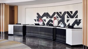 Uma mesa de recepção com design moderno, apresentando um padrão geométrico na parede e um balcão elegante e curvo.