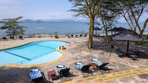 Área da piscina com espreguiçadeiras e guarda-sóis, cercada por árvores e vista para o mar.