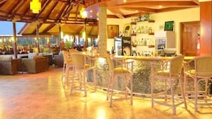 Uma área de bar com cadeiras de vime e um balcão, cercada por uma estrutura de madeira com piso de azulejos.