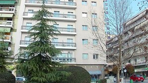 Um edifício de vários andares com varandas, uma árvore verde e um arbusto em primeiro plano.