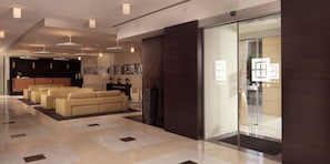 Um lobby moderno com área de estar, balcão de recepção e entrada por porta de vidro.