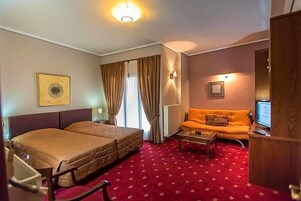 Quarto de hotel com uma cama de casal, um sofá, uma mesinha e uma televisão.