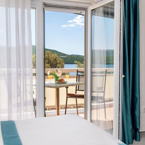 Quarto com uma cama, uma mesa com bebidas e vista para um lago e colinas.