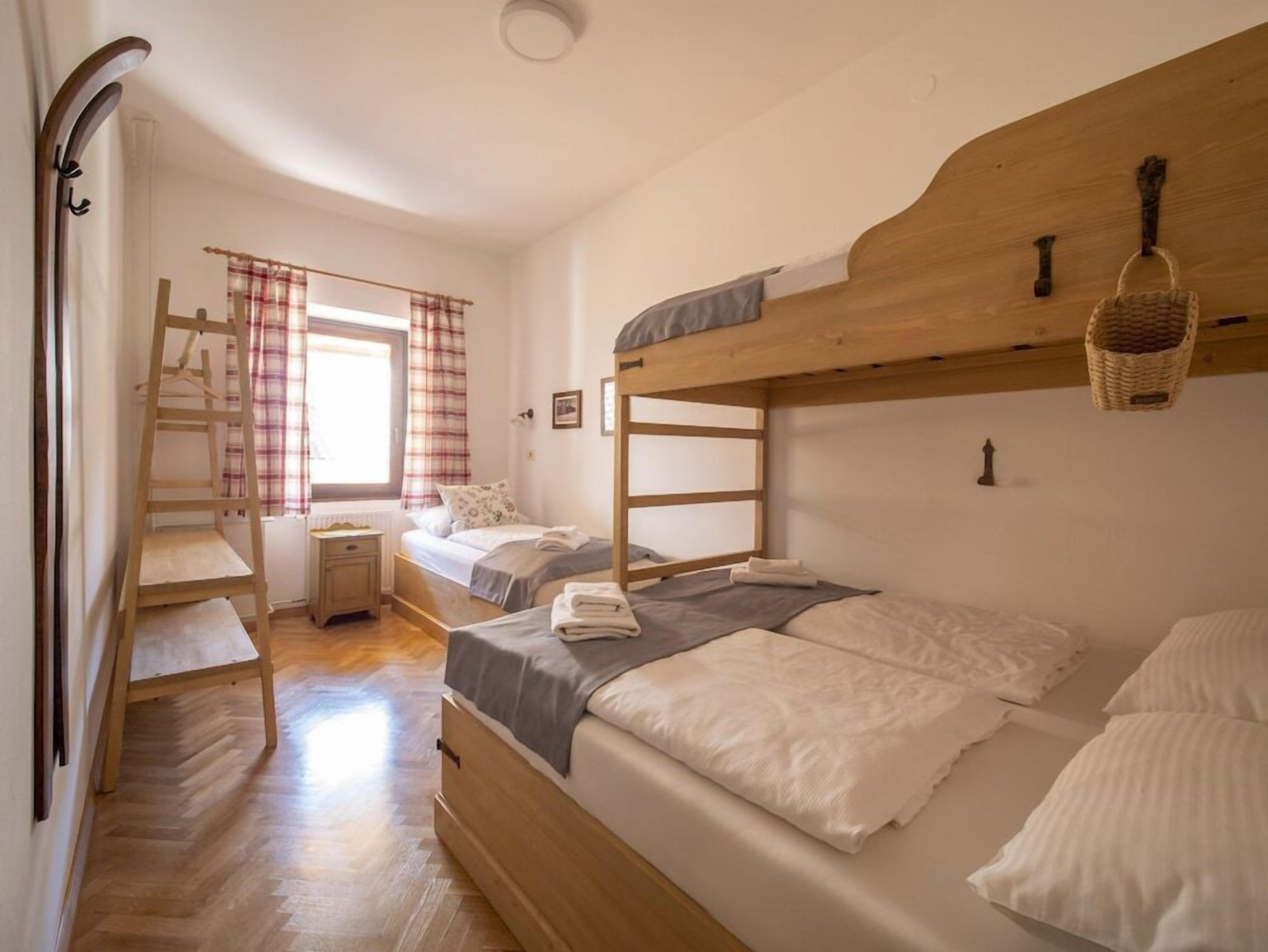 Quarto com beliche, escada de madeira, janela com cortinas e uma mesinha de cabeceira.