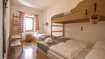 Quarto com beliche, escada de madeira, janela com cortinas e uma mesinha de cabeceira.