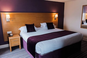 Quarto de hotel com cama, mesa de cabeceira, abajur e espelho na parede.