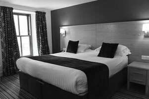 Quarto de hotel com uma cama grande, duas mesas de cabeceira e uma janela com cortinas.