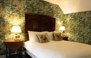 Quarto com uma cama grande, duas luminárias de cabeceira, papel de parede floral e cabeceira de madeira.