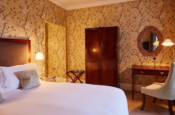 Quarto de hotel com uma cama grande, um guarda-roupa de madeira, uma escrivaninha com espelho e uma cadeira.