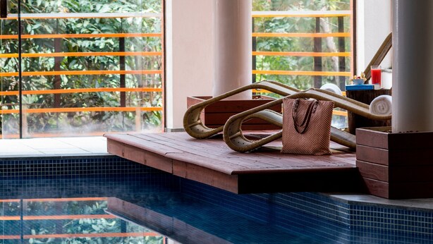 Piscina com borda azulejada, cadeira de vime e uma pequena mesa com um copo de bebida vermelha.