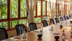 Sala de conferências com uma mesa comprida, cadeiras e vista para o verde através de grandes janelas.