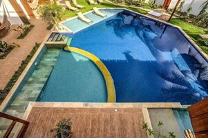 Piscina com borda curva, rodeada por um deck de madeira e uma área gramada com espreguiçadeiras.