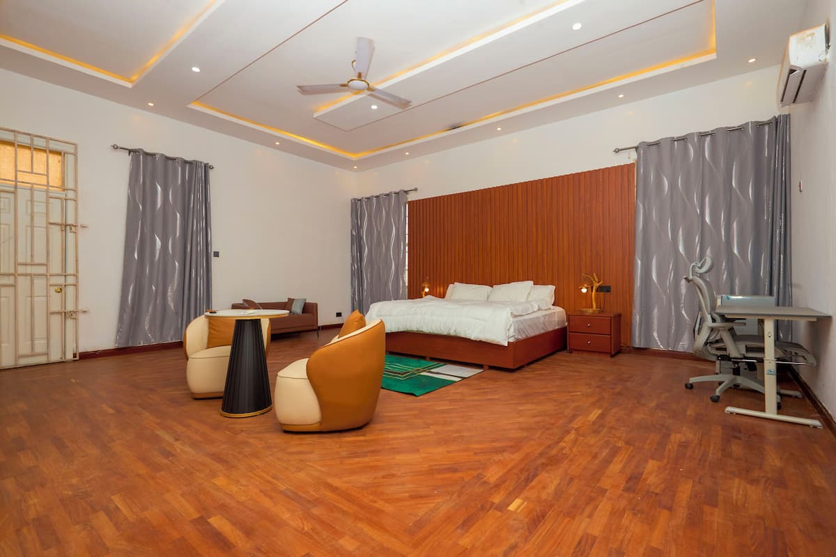 Quarto moderno com piso de madeira, uma cama, escrivaninha, cadeira e ventilador de teto.