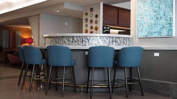 Uma área de bar com quatro banquetas azuis, um balcão de bar estampado e uma cozinha com armários e micro-ondas.