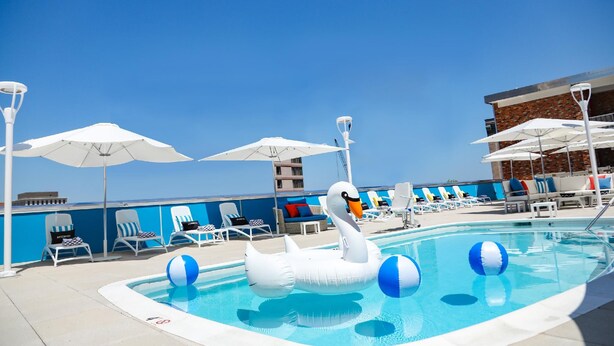 Uma piscina com um flutuador de cisne, cadeiras de descanso, guarda-sóis e vista para o oceano.